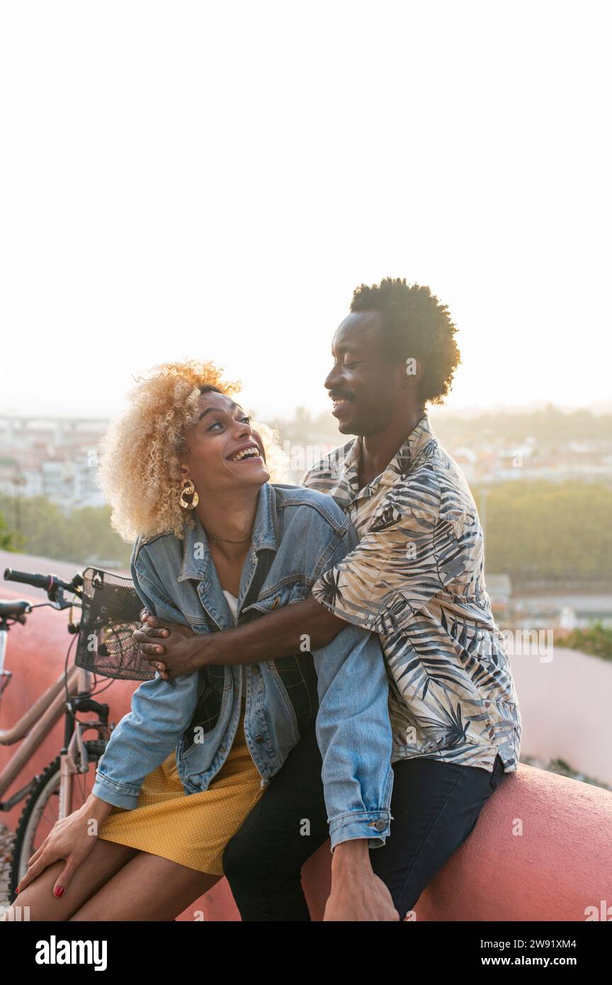 Smiling boyfriend embracing transgender woman sitting on wall Stock ...