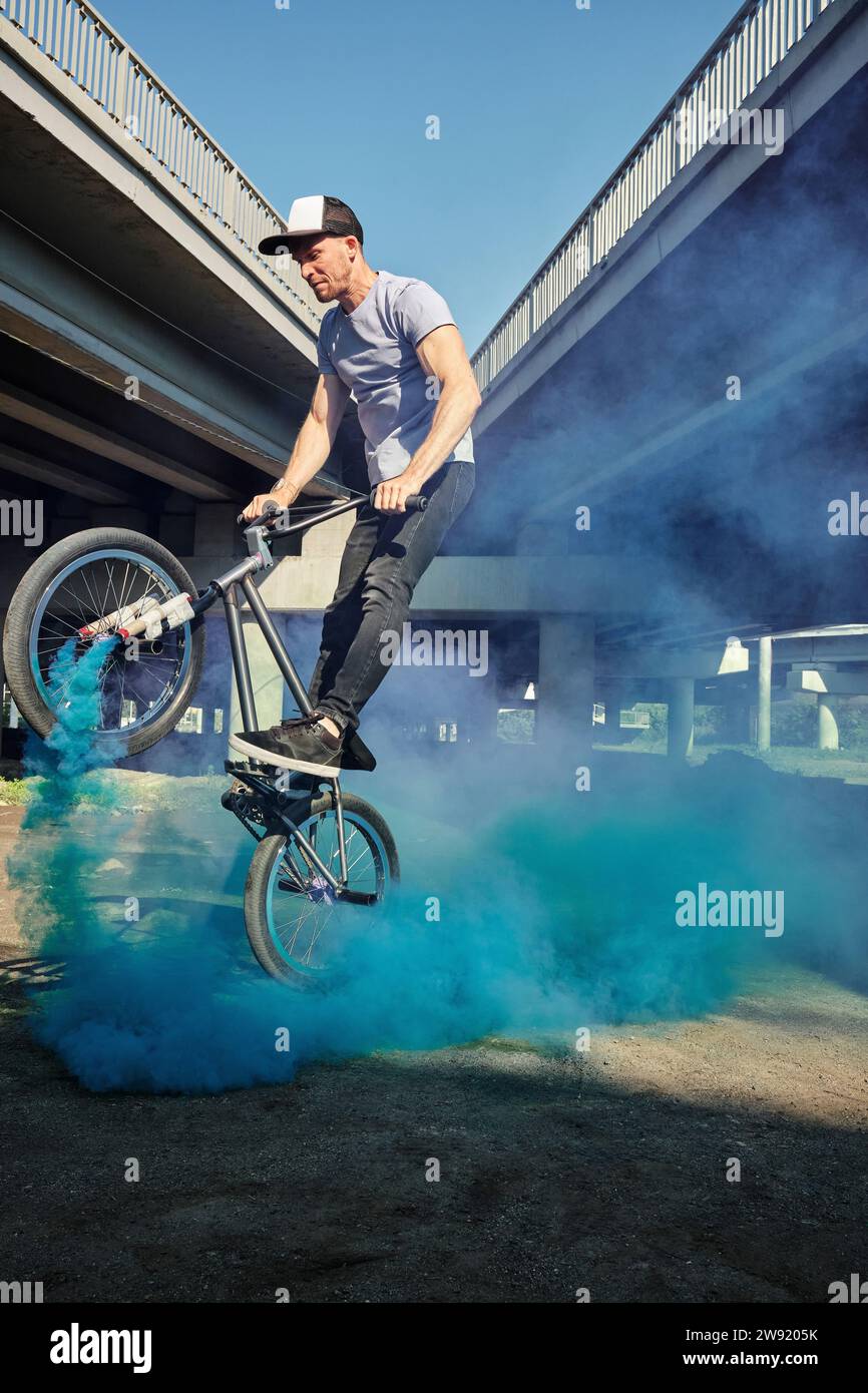 Man doing stunt with BMX bike emitting blue smoke near bridge Stock ...
