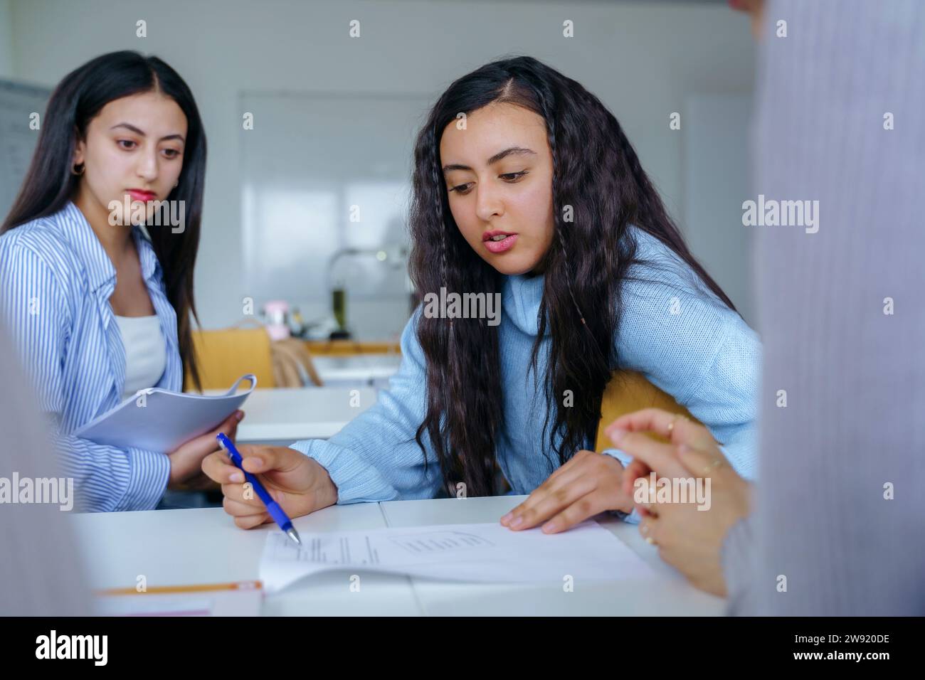 Woman with pen reading notes and explaining to friends in classroom ...