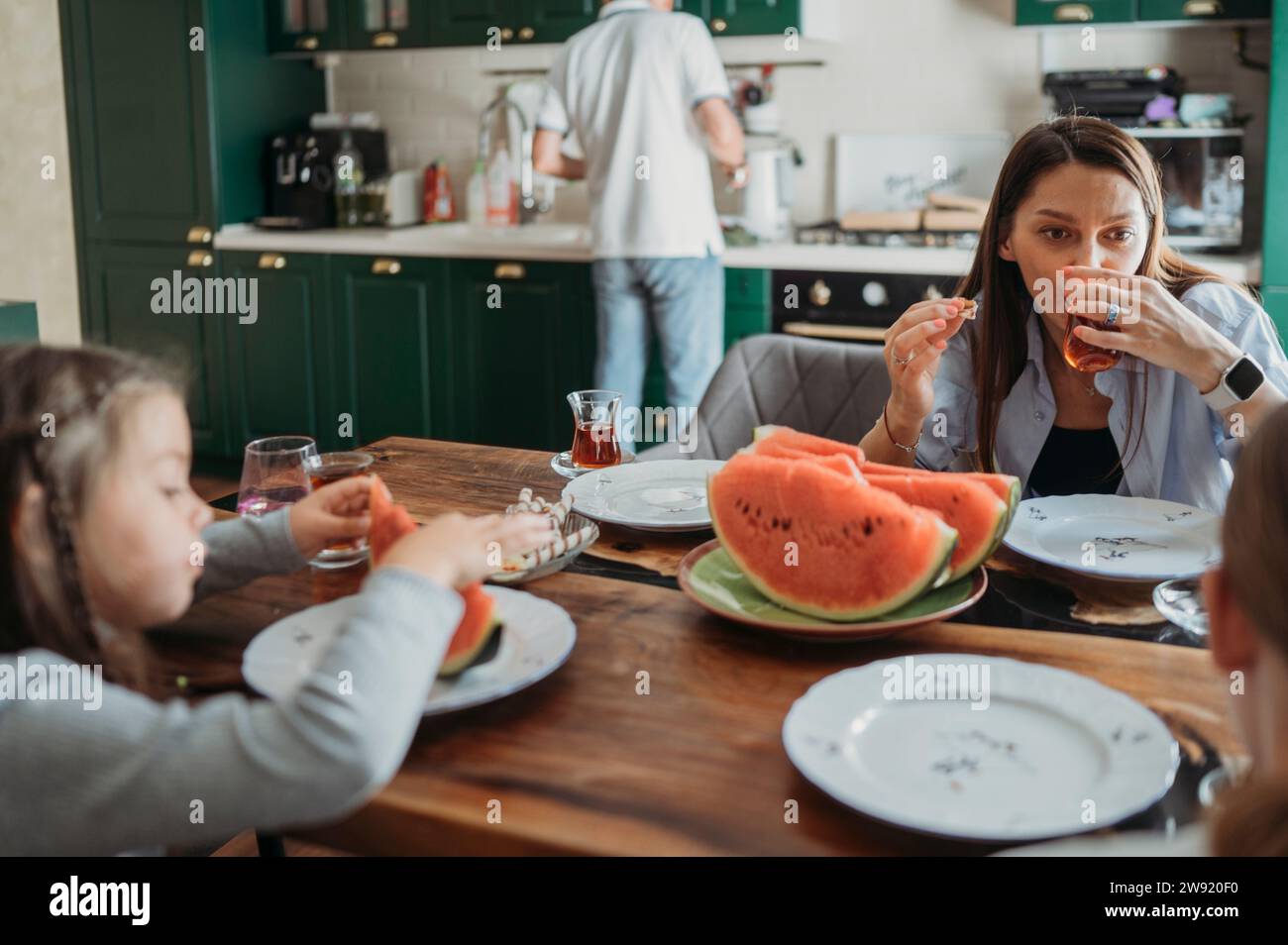 Family having lunch at table with man cooking in background Stock Photo ...