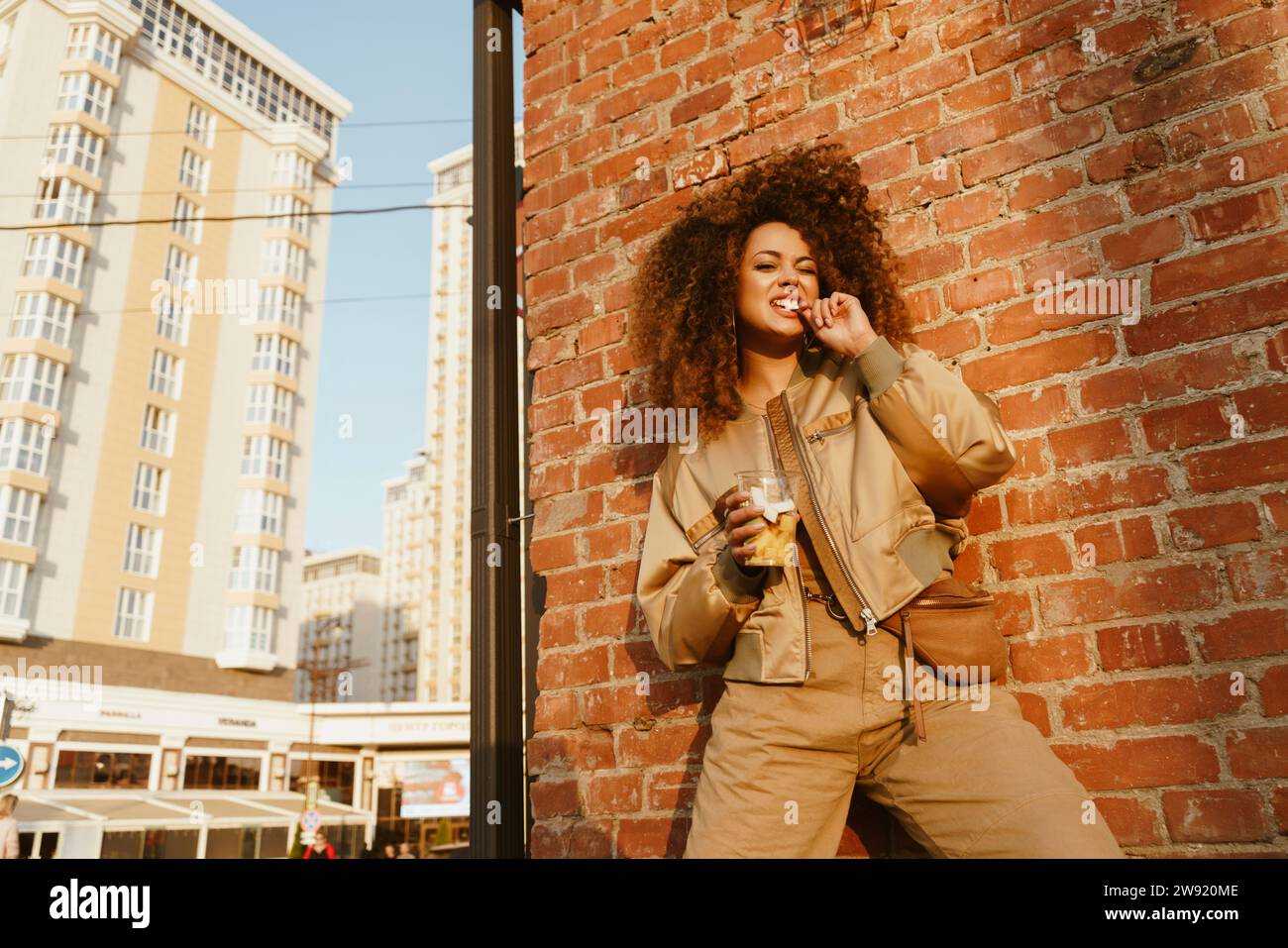 Fashionable woman eating fruit salad in front of brick wall Stock Photo ...