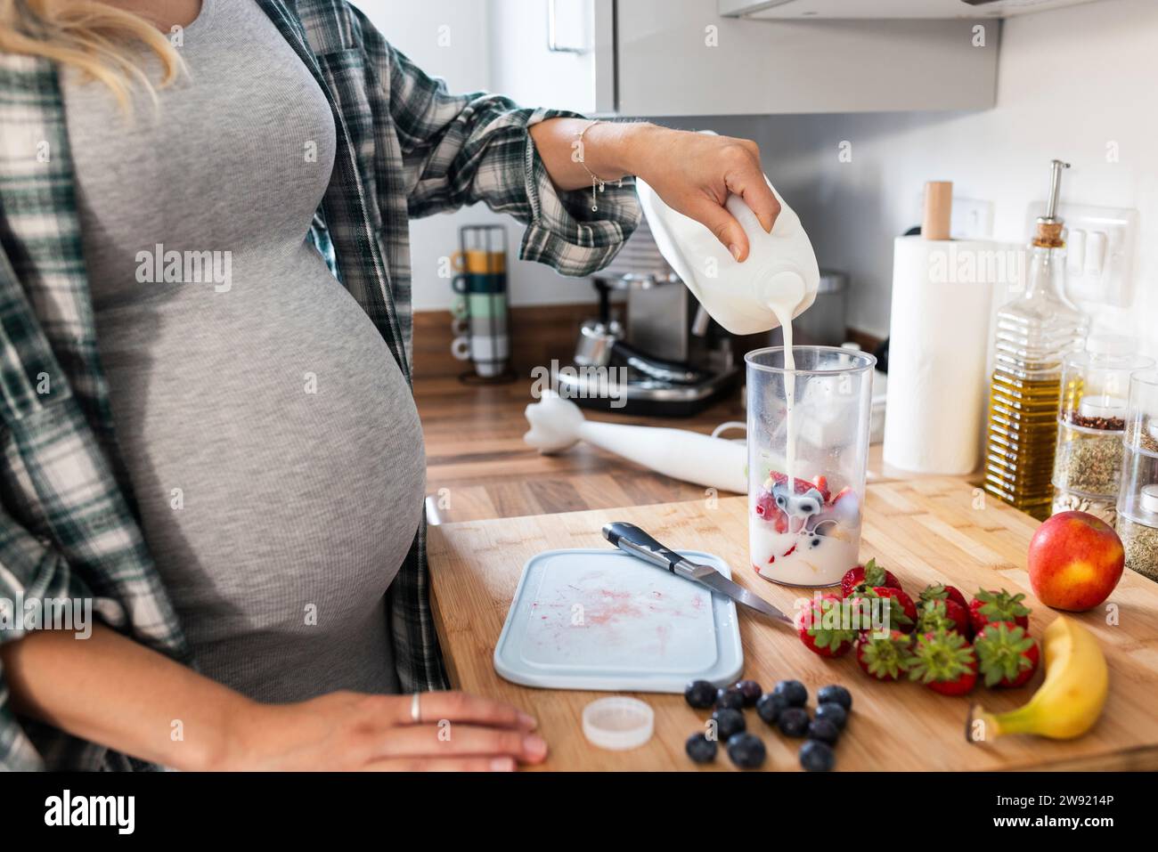 Pregnant woman pouring milk in measuring cup and preparing milkshake ...
