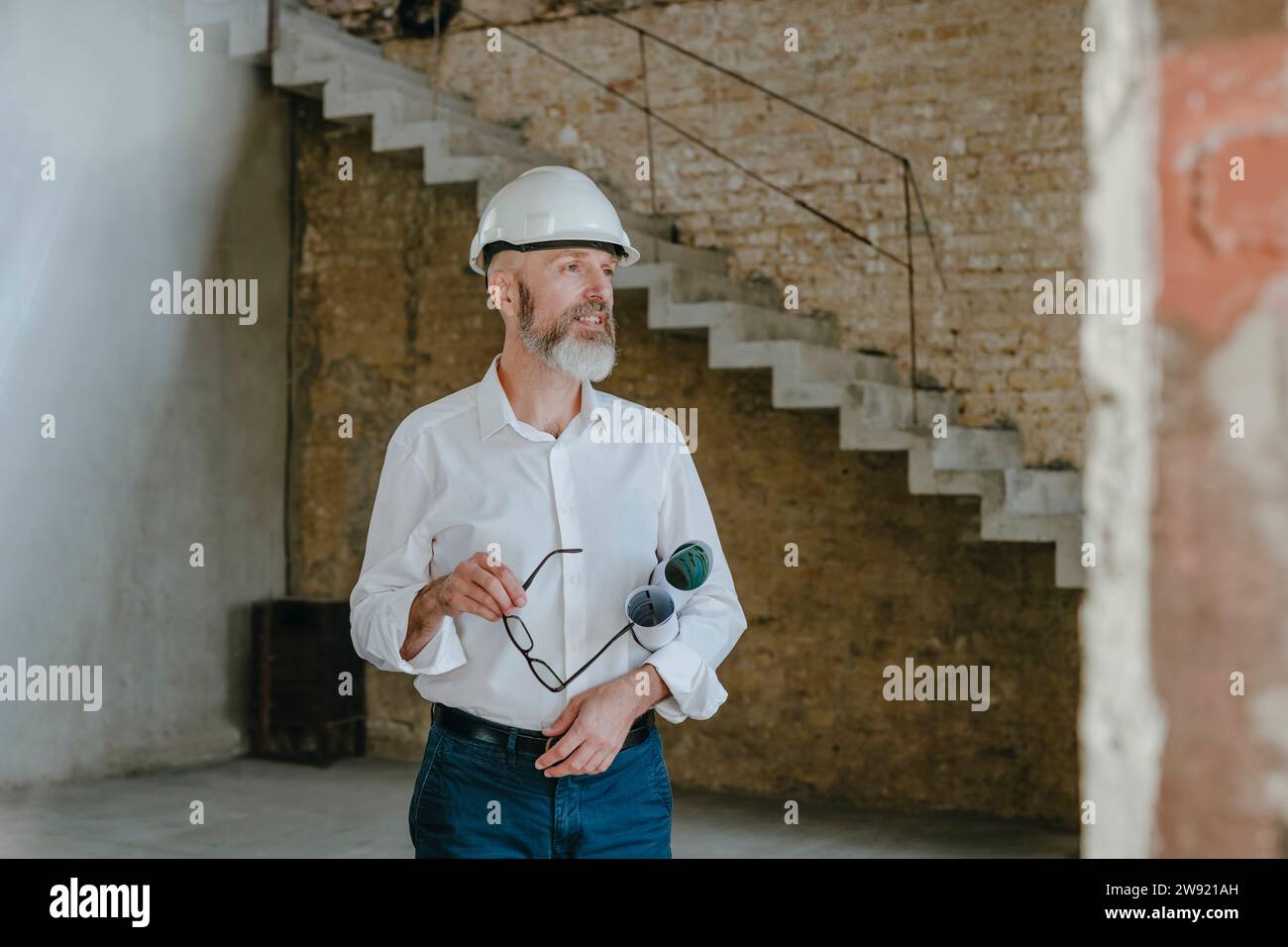Happy architect standing with eyeglasses and documents at construction ...