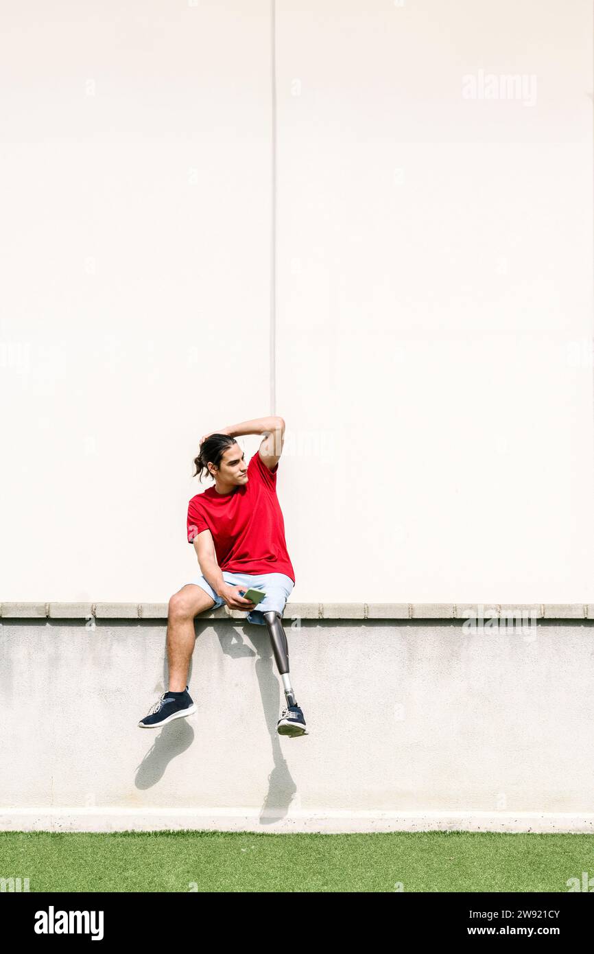 Man sitting with prosthetic leg and holding smart phone in front of ...