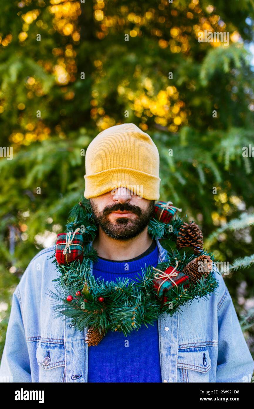 Man covering eyes with knit hat and wearing Christmas wreath around ...