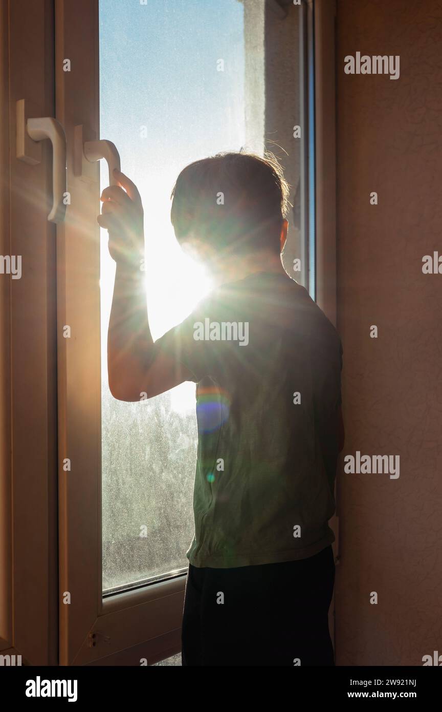 Boy looking through window on sunny day Stock Photo - Alamy
