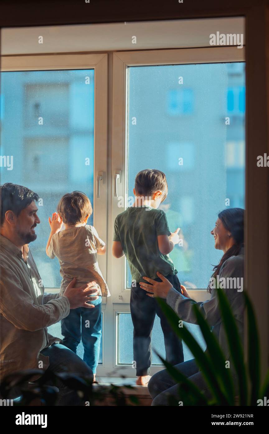 Parents holding children looking outside through window at home Stock ...
