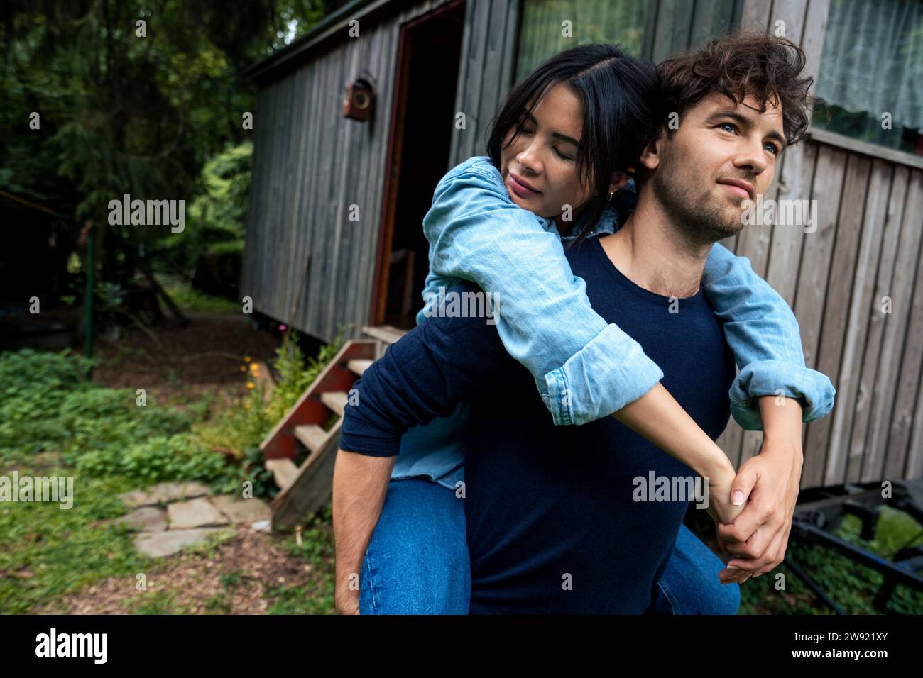 Smiling man giving piggyback ride to woman in front of wooden cabin ...