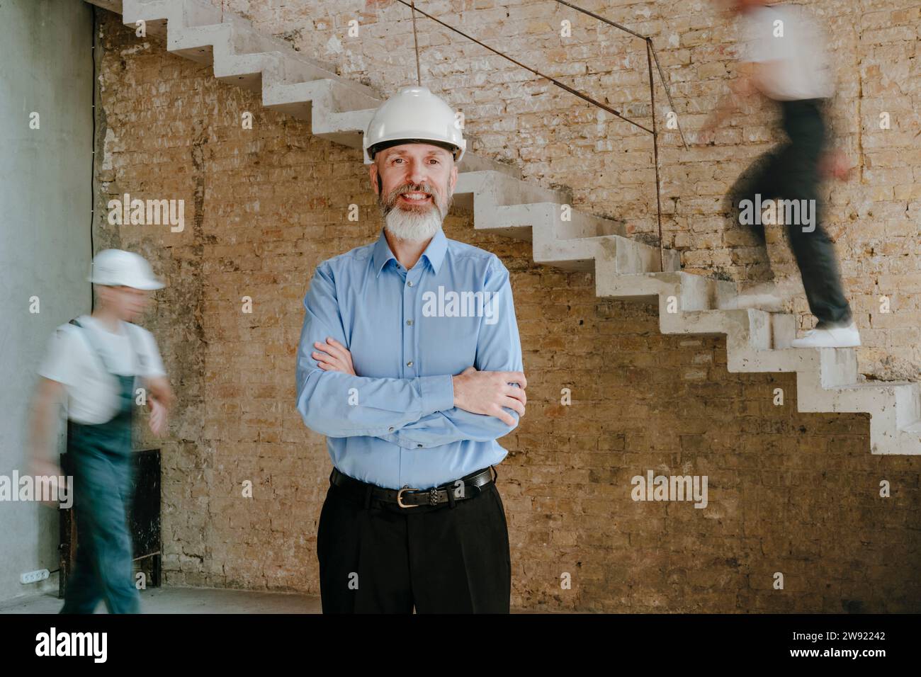 Happy architect standing with arms crossed at construction site Stock ...