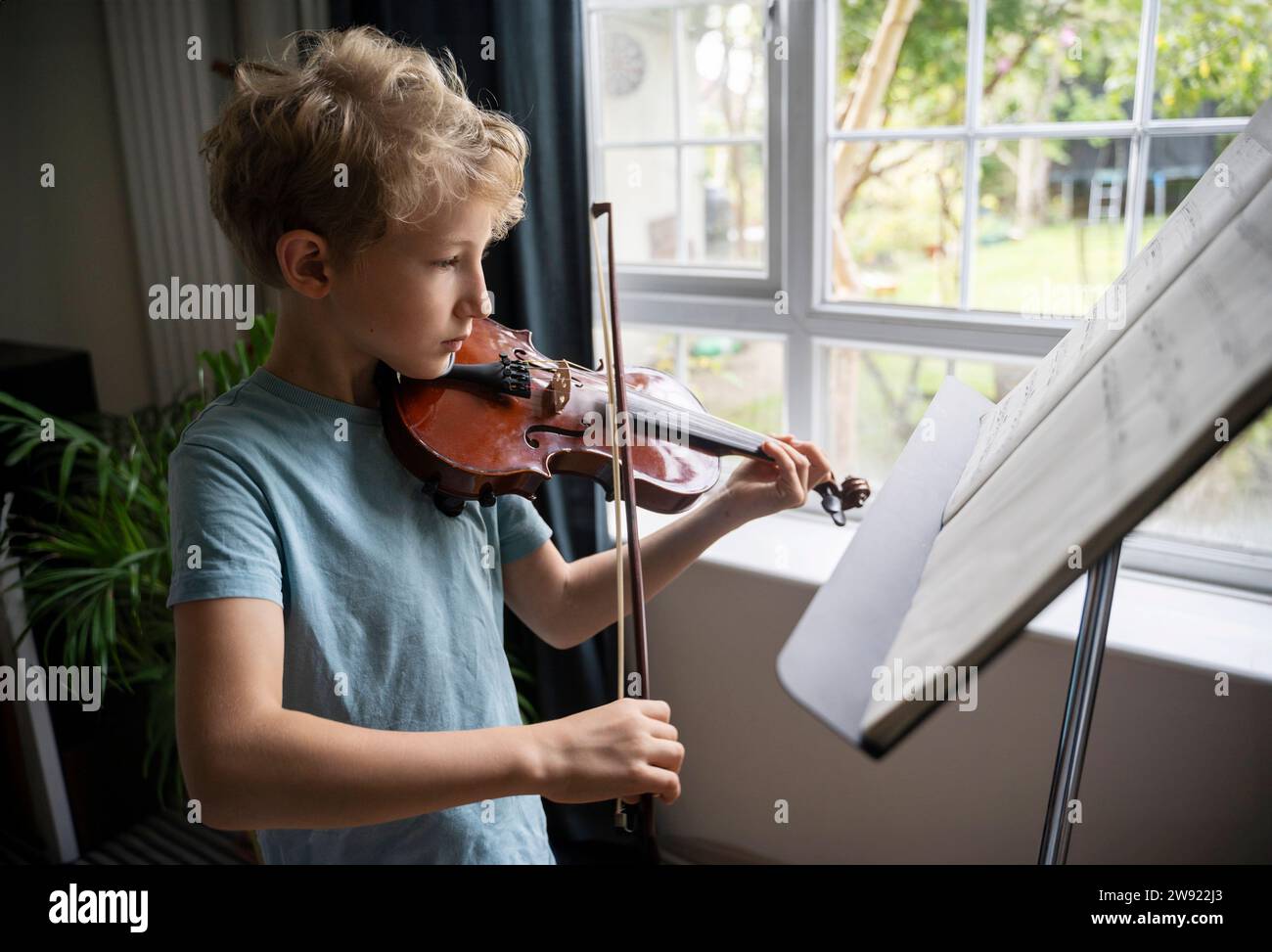 Elementary boy practicing to play violin near window at home Stock ...