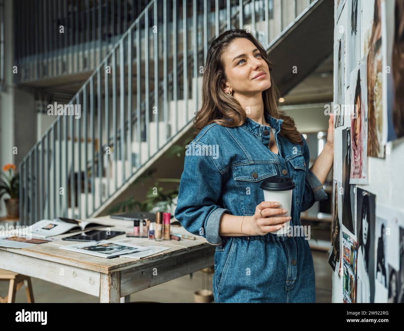 Smiling influencer looking at photographs on wall in studio Stock Photo ...
