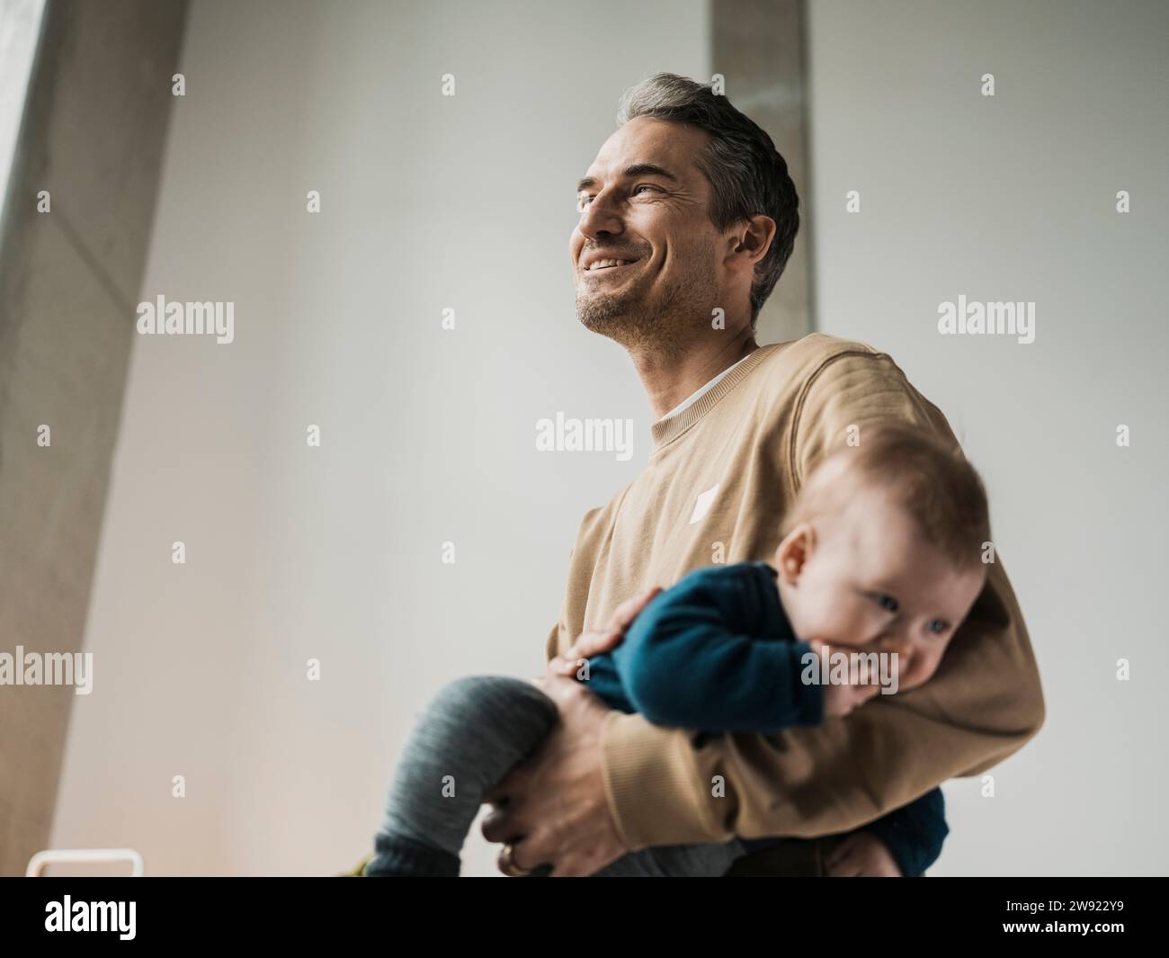 Smiling man carrying baby boy at home Stock Photo - Alamy