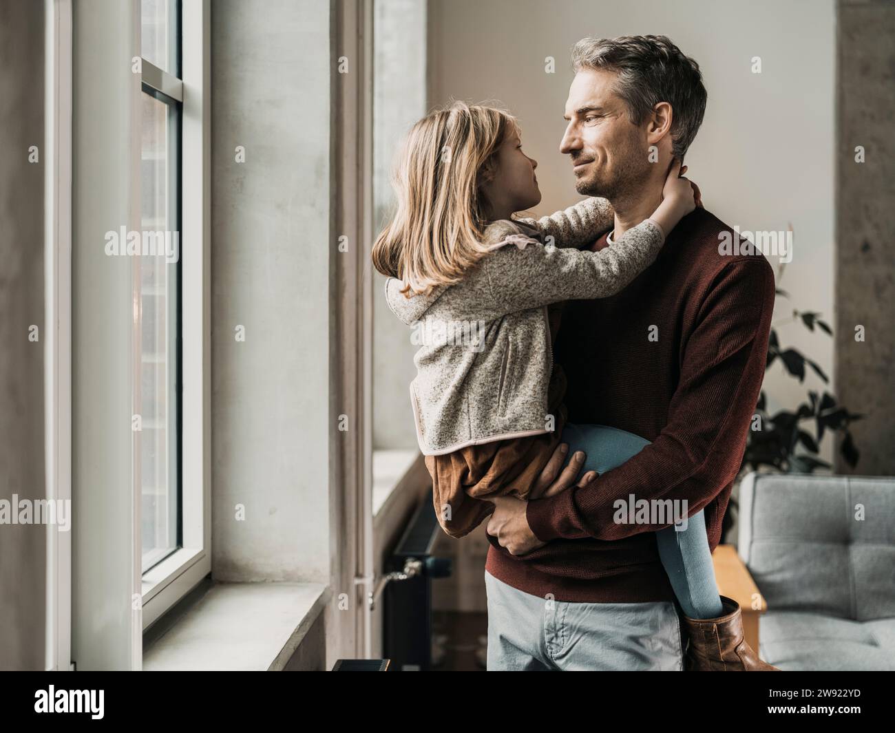Smiling father holding daughter in arms near window at home Stock Photo ...