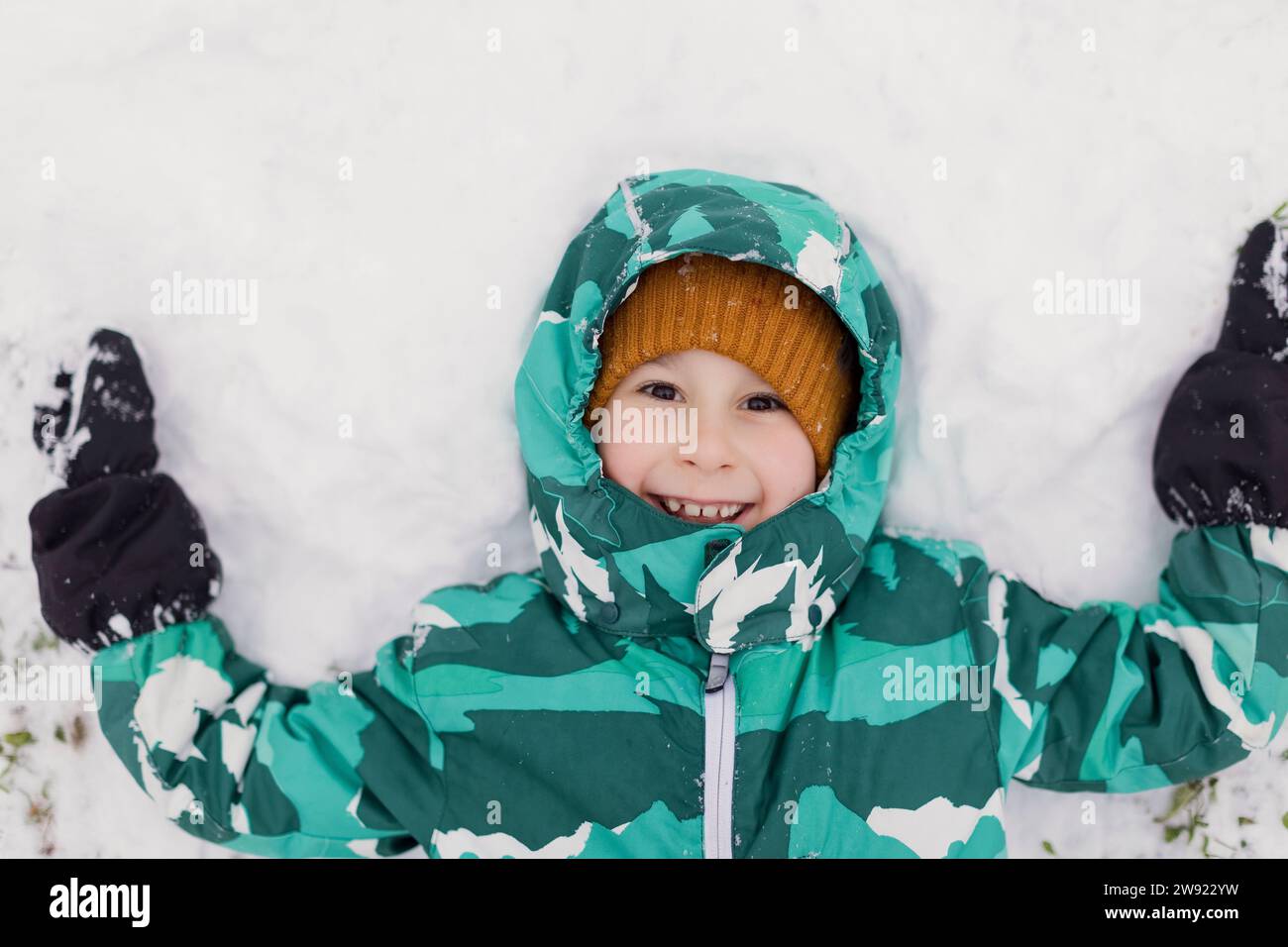 Elementary boy wearing jacket and lying on snow Stock Photo - Alamy