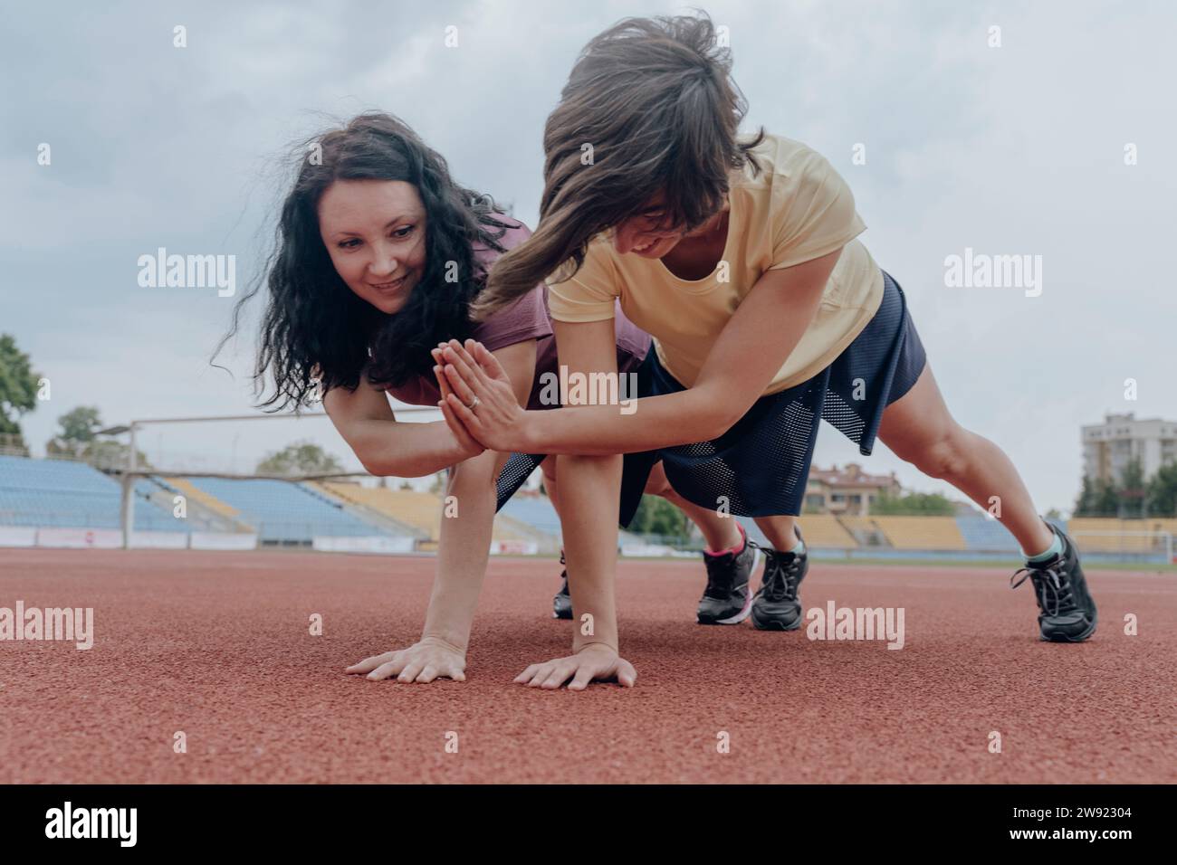 Friends doing push-ups and giving high-five on running track at stadium ...