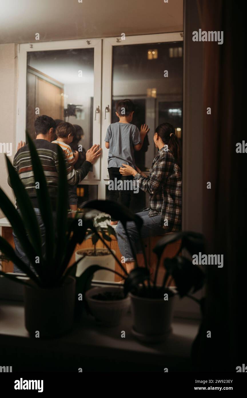 Family looking outside through window at home Stock Photo - Alamy