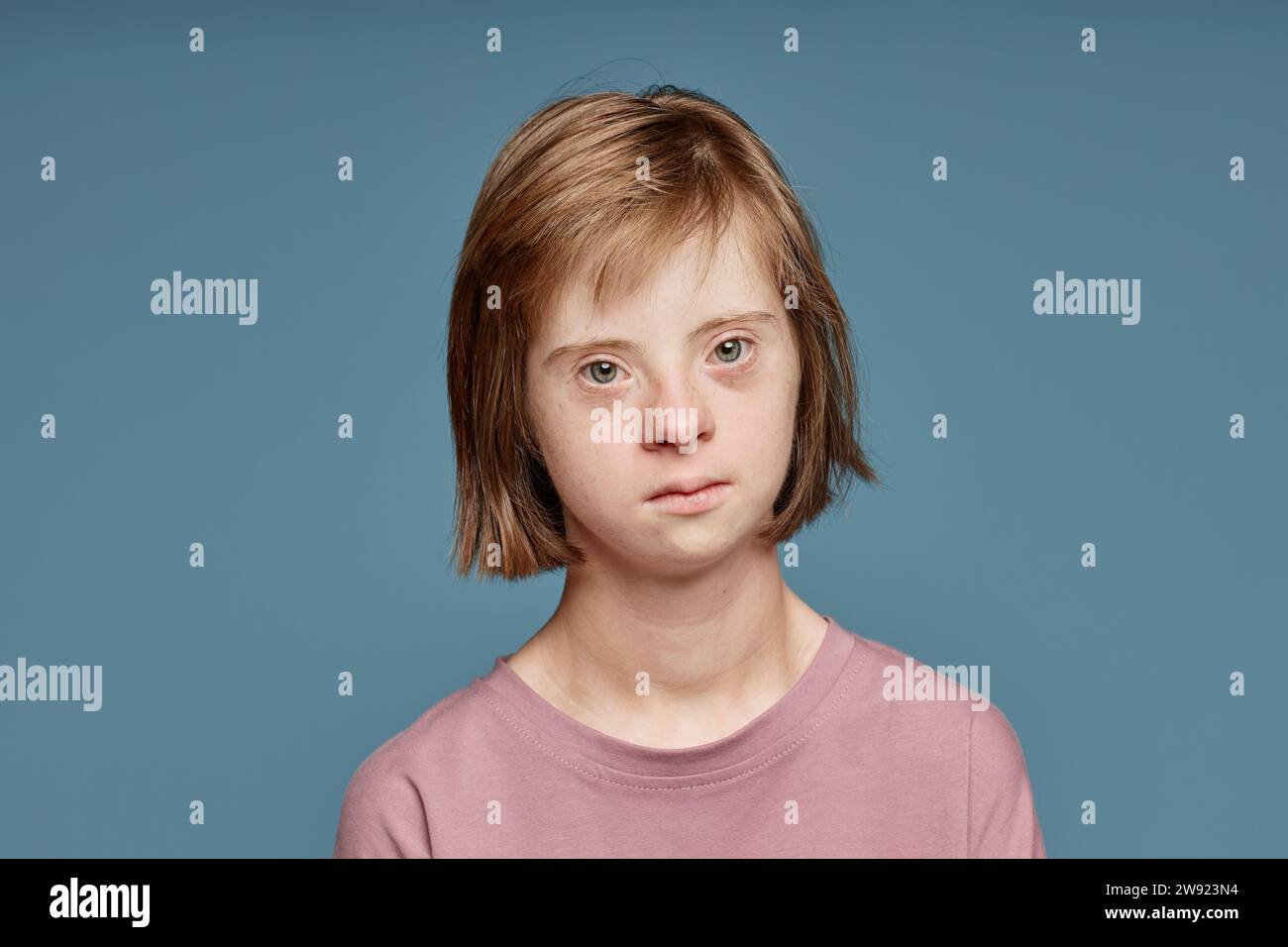 Sad girl with Down syndrome against blue background Stock Photo - Alamy