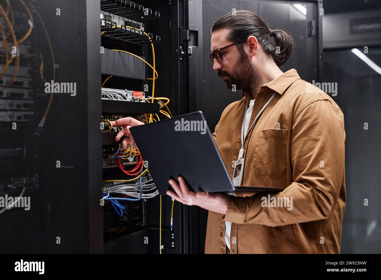 Engineer holding laptop and examining cables in server room Stock Photo ...