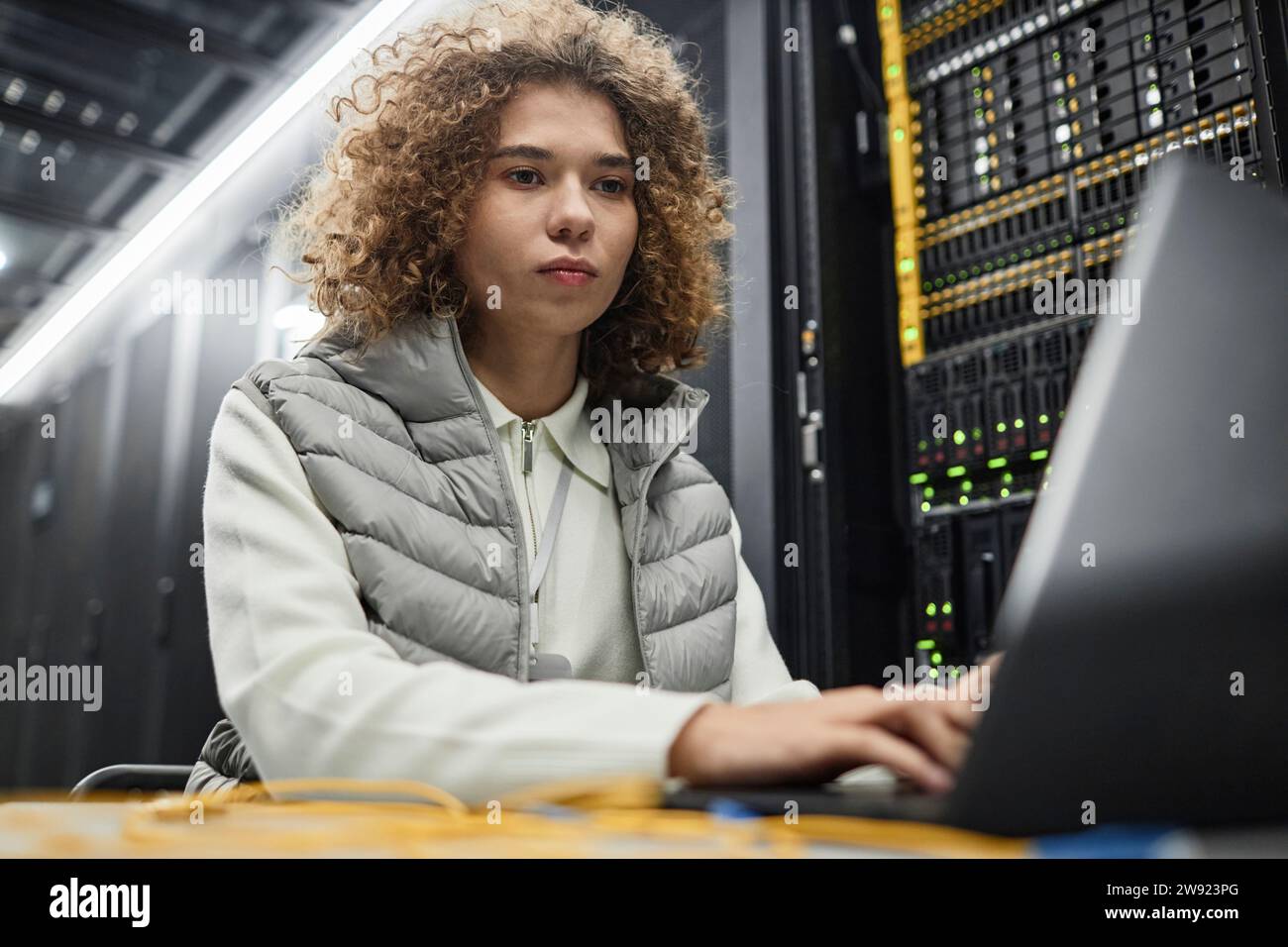 Engineer with curly hair working on laptop in server room Stock Photo ...