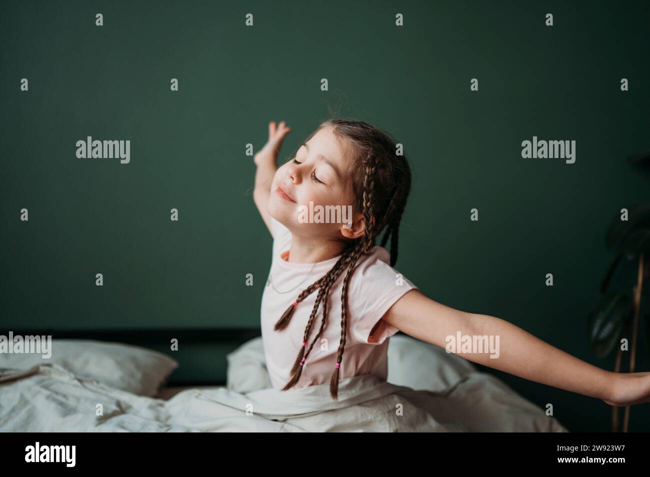 Happy girl with braided hair stretching on bed at home Stock Photo - Alamy