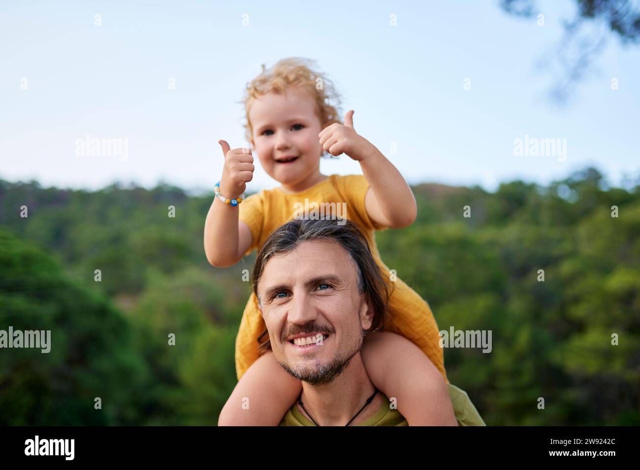 Cute girl showing thumbs up sitting on father's shoulder Stock Photo ...