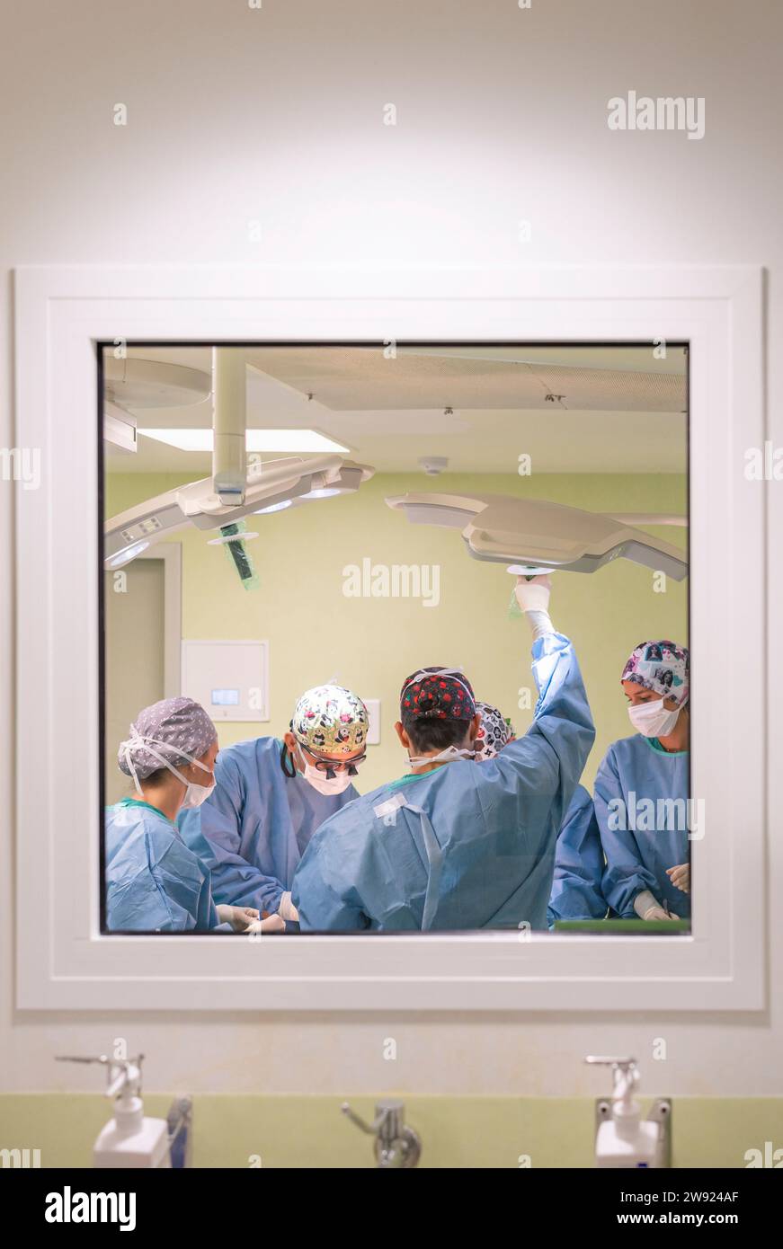 Surgeons performing surgery seen through glass in hospital Stock Photo ...