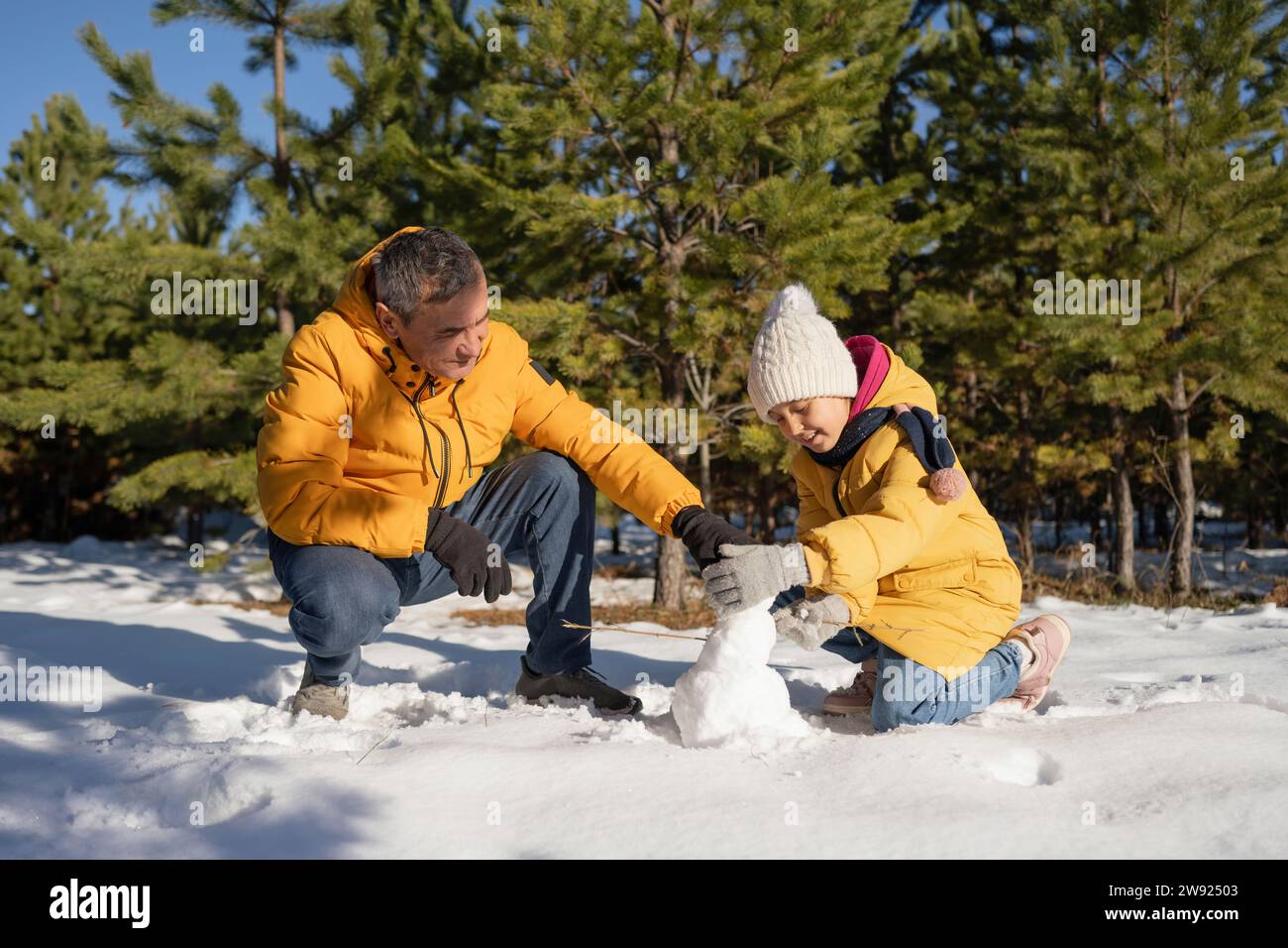 Father and daughter building snowman with snow near trees in winter ...