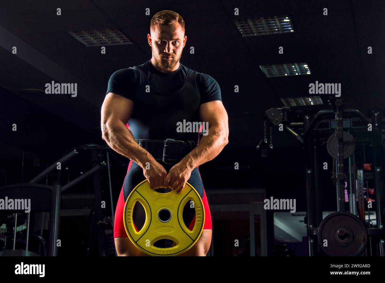 Huge weightlifter stands with a weight in his hands in the gym Stock ...