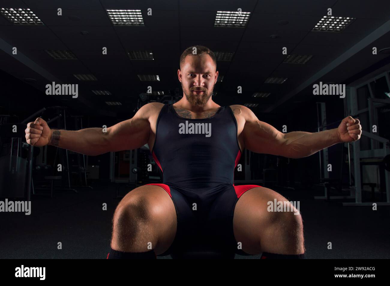 The weightlifter sits on a bench in the gym with arms outstretched and ...