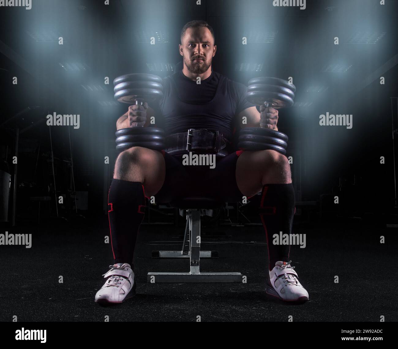 Professional weightlifter sits on a bench in the gym with two dumbbells ...