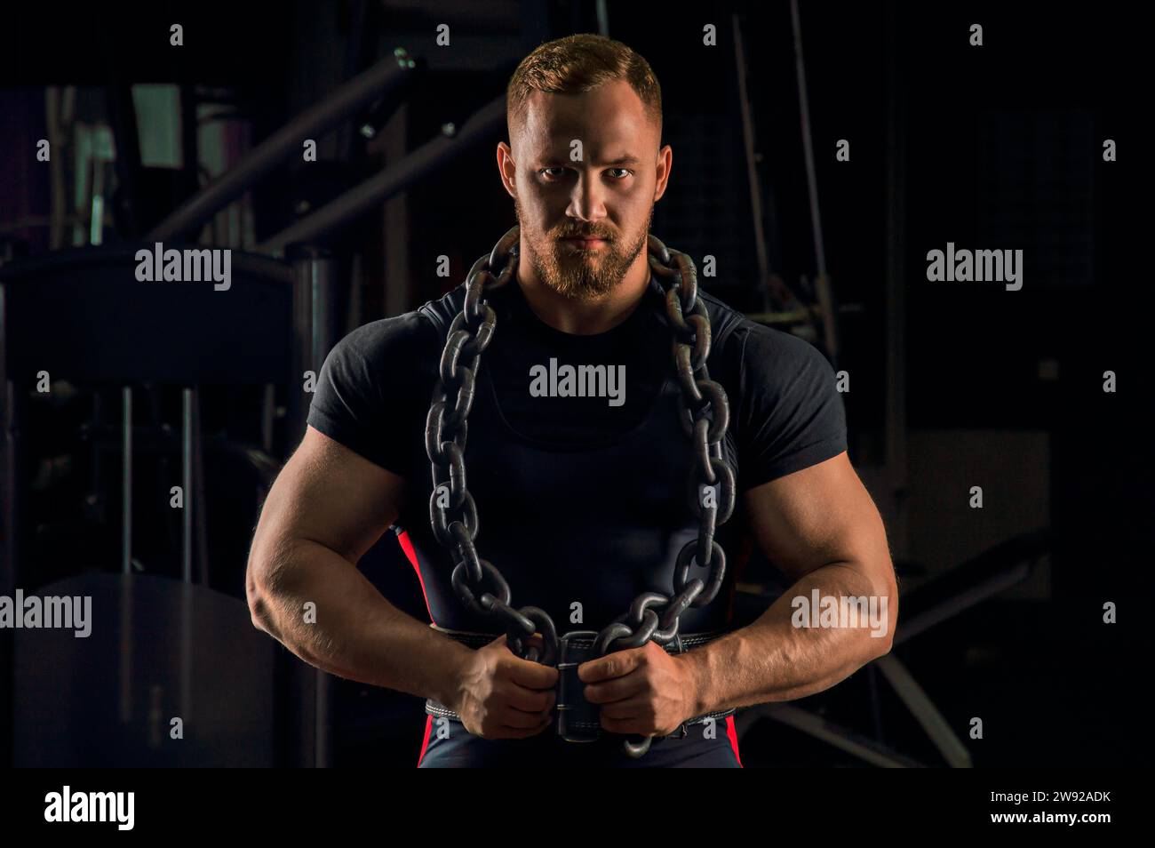 Handsome athlete with a chain around his neck stands in the gym and ...