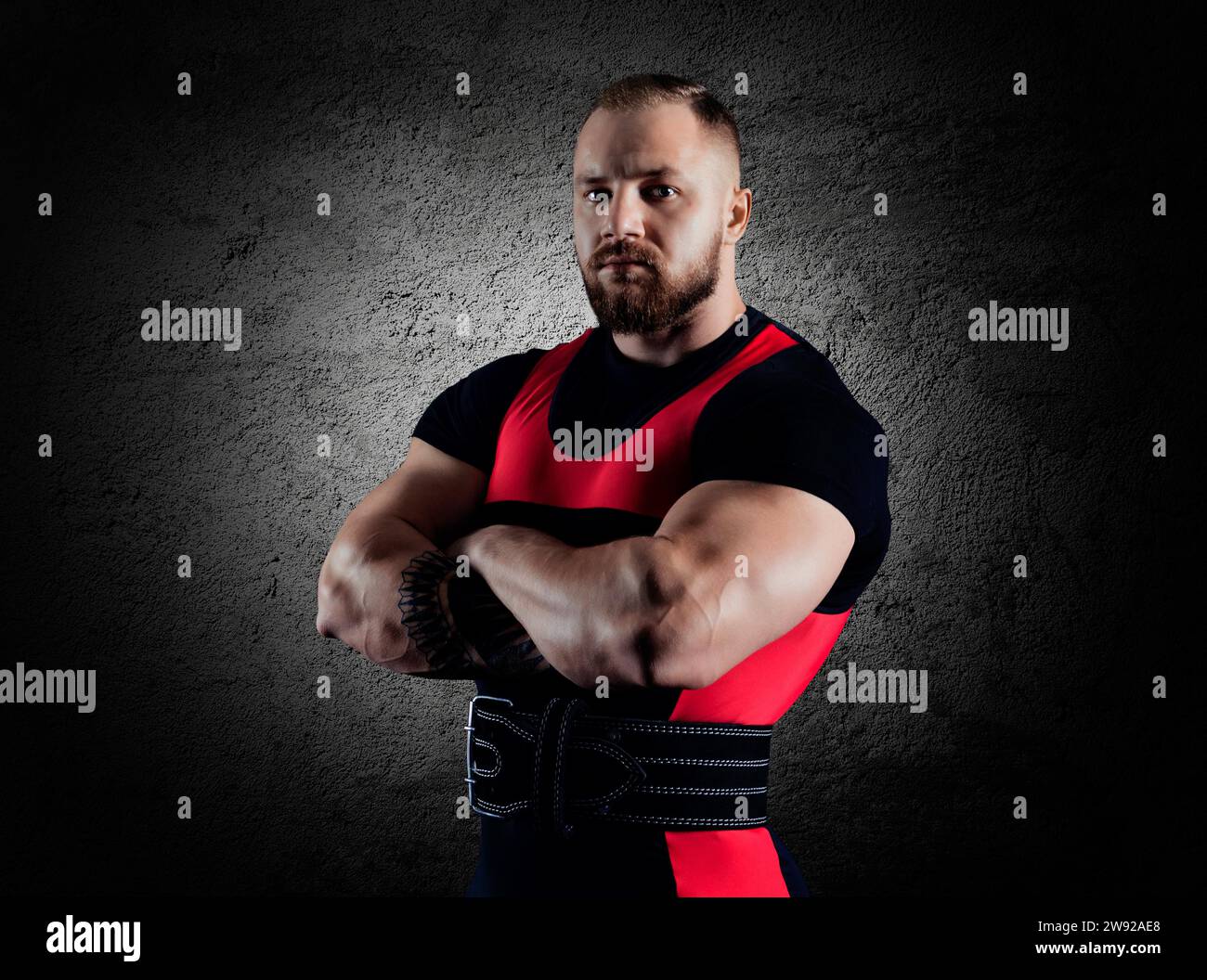 The weightlifter stands in a menacing pose with crossed huge arms and ...