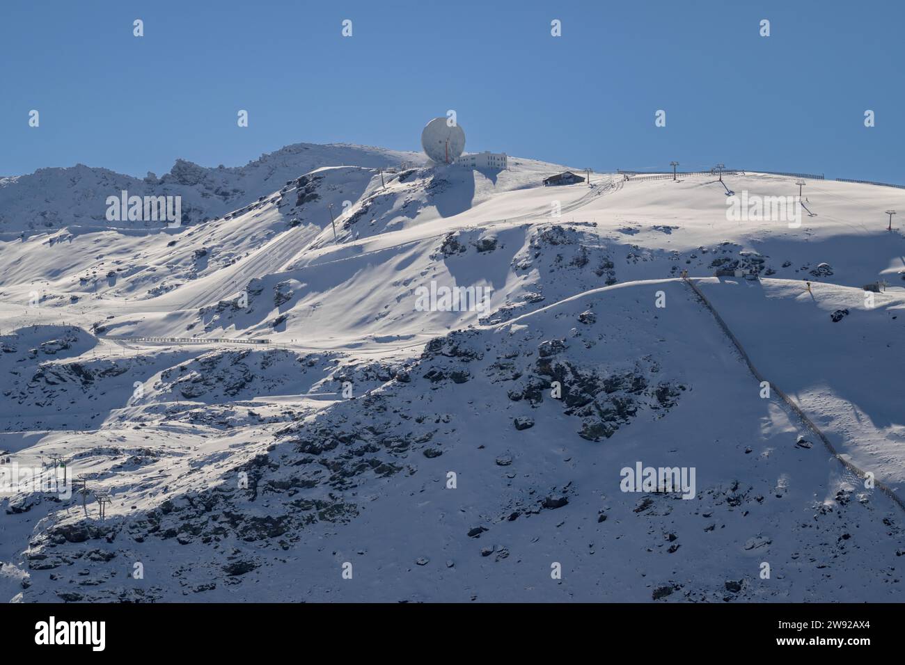 Snow-covered mountain under a clear blue sky with a radar antenna at ...
