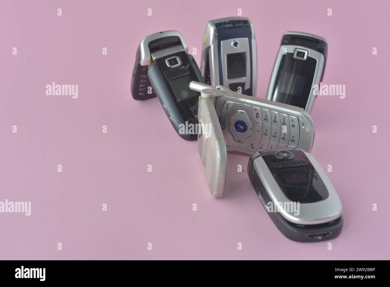 Two vintage flip phones open and standing among other models on a pink ...