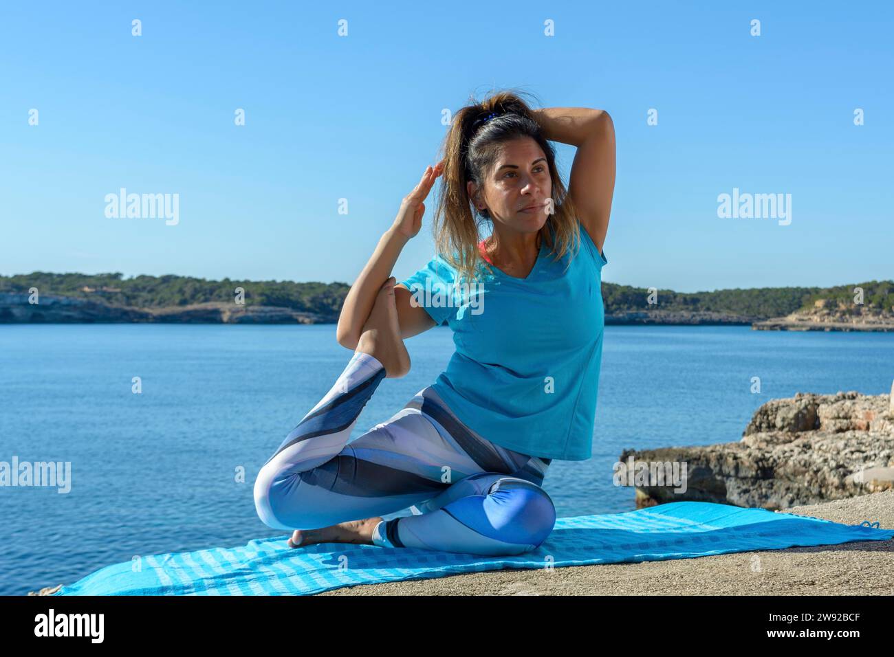 Middle-aged fitness woman outdoors in front of the sea does yoga ...