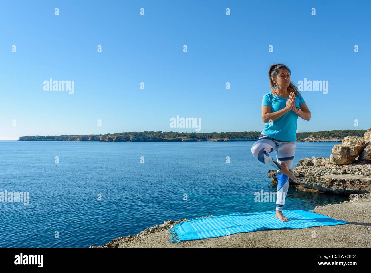 Middle-aged fitness woman outdoors in front of the sea does yoga ...