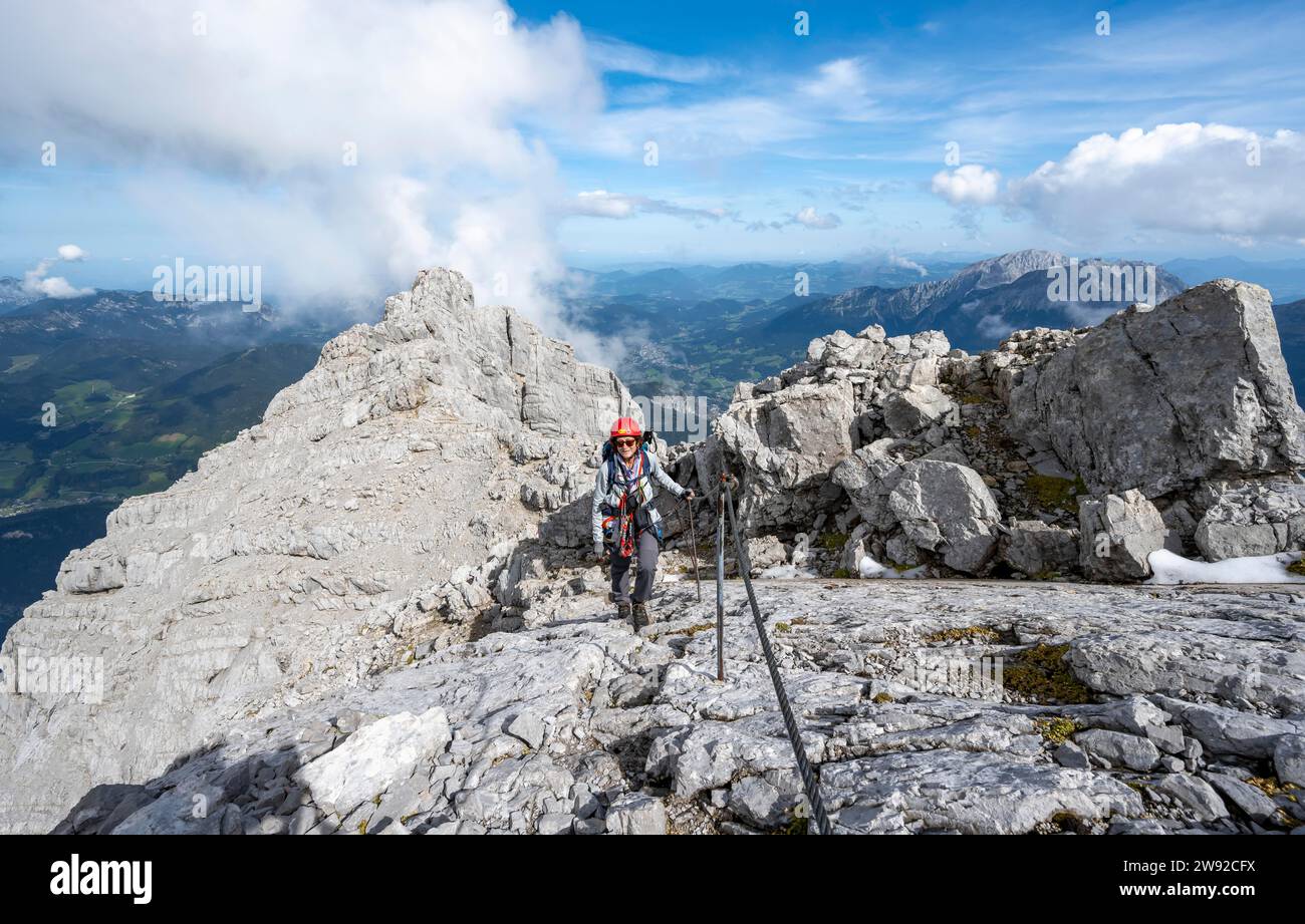 Climber on a via ferrata secured with a steel cable, narrow rocky ridge ...