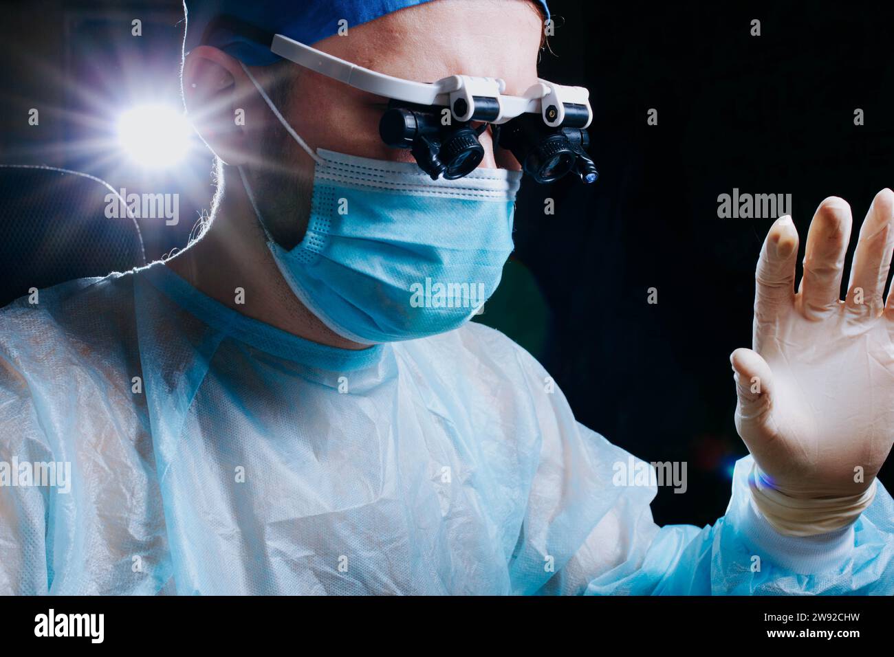 Surgeon wearing binocular magnifying glasses operates on a patient in a ...