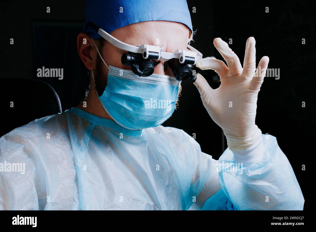 Surgeon wearing binocular magnifying glasses operates on a patient in a ...
