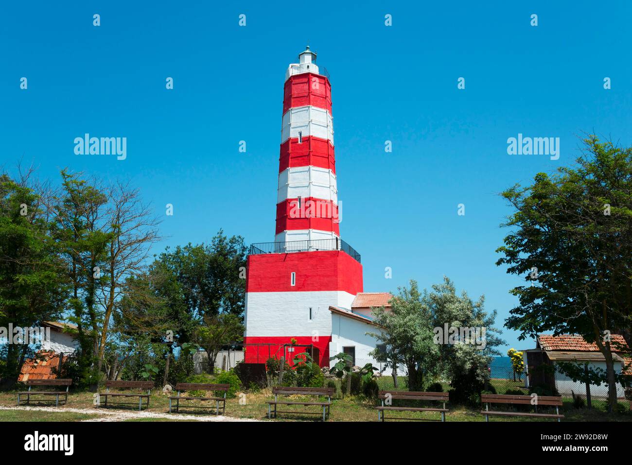Red and white striped lighthouse surrounded by trees and a meadow under ...