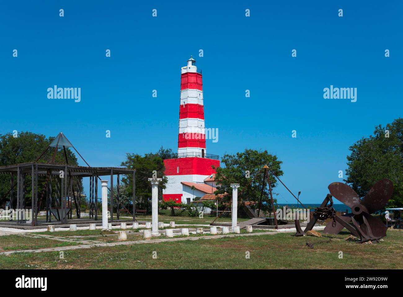 Red and white lighthouse under a blue sky next to green areas and a ...