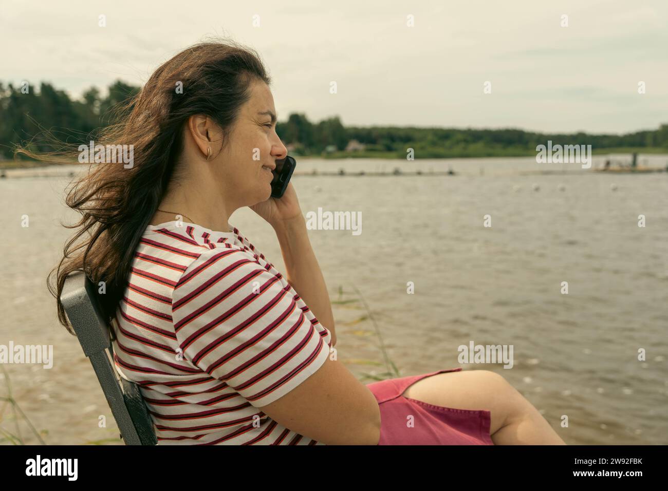 A middle-aged woman with long flowing hair sitting by the serene ...