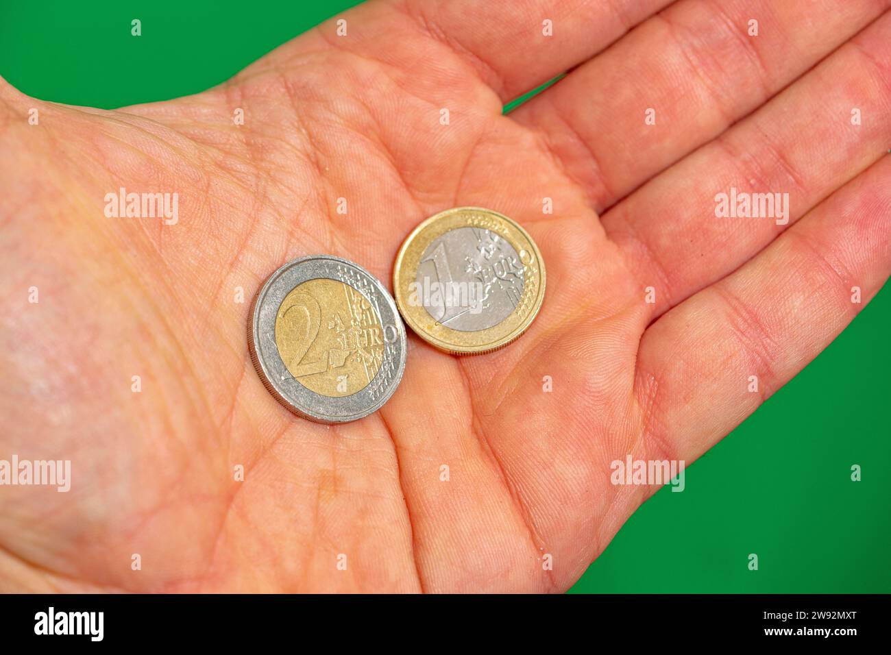 coin face of 1 and 2 euro on the palm. green background Stock Photo - Alamy