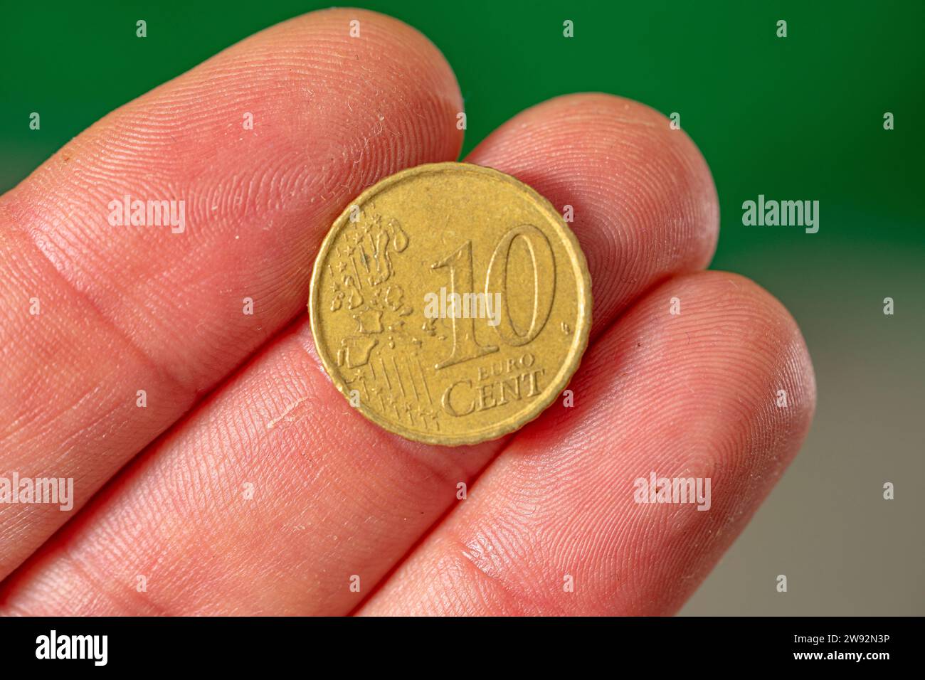 coin face of 10 euro cents in the fingers of the hand. green background ...