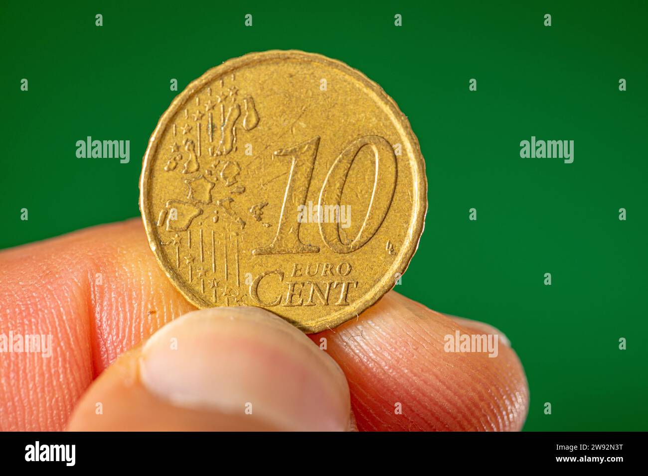coin face of 10 euro cents in the fingers of the hand. green background ...