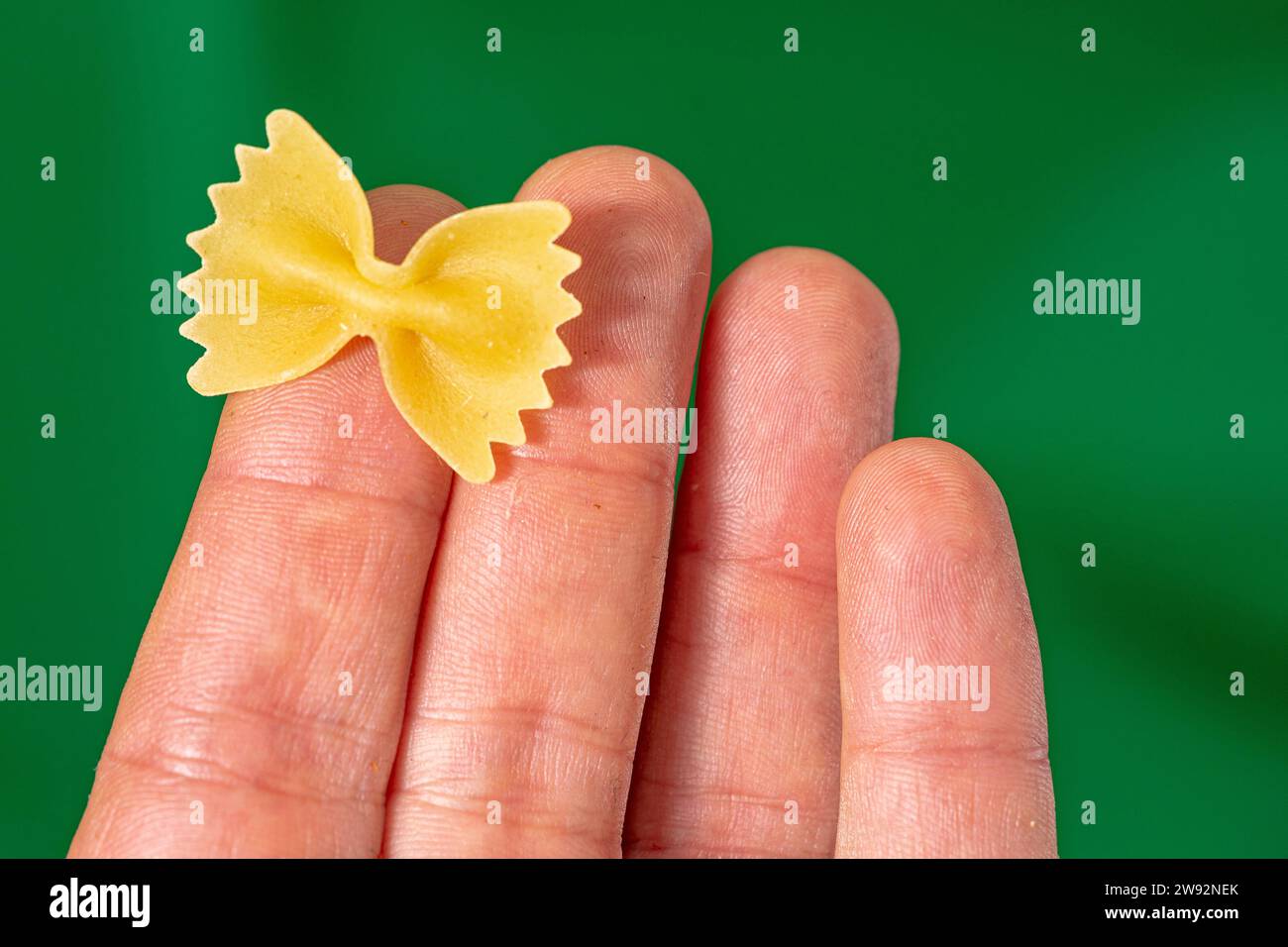loop-shaped food wheat pasta between fingers under green background ...