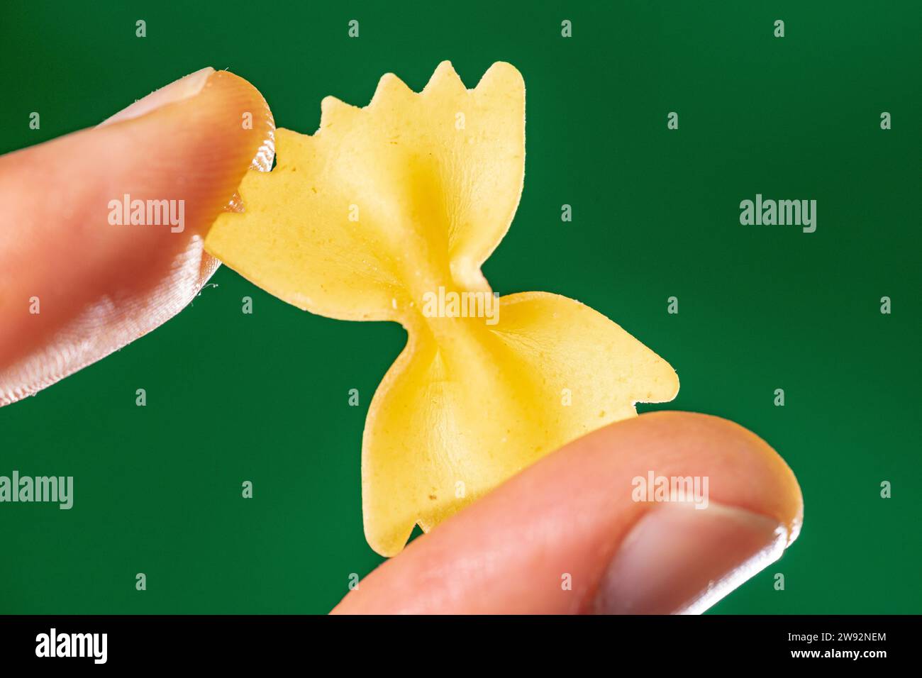 loop-shaped food wheat pasta between fingers under green background ...