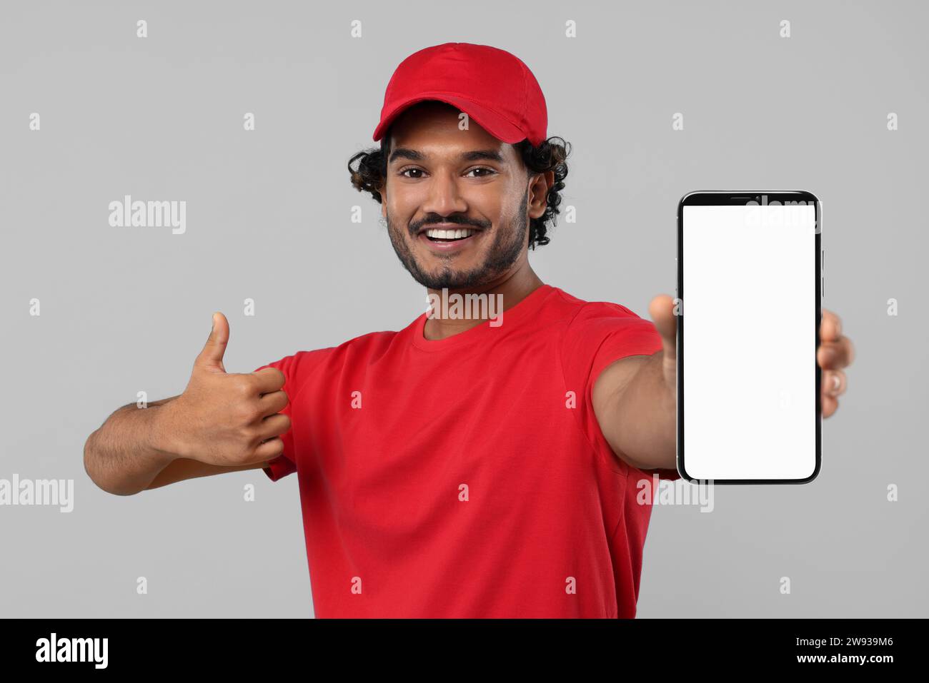 Happy courier holding smartphone with empty screen and showing thumbs ...