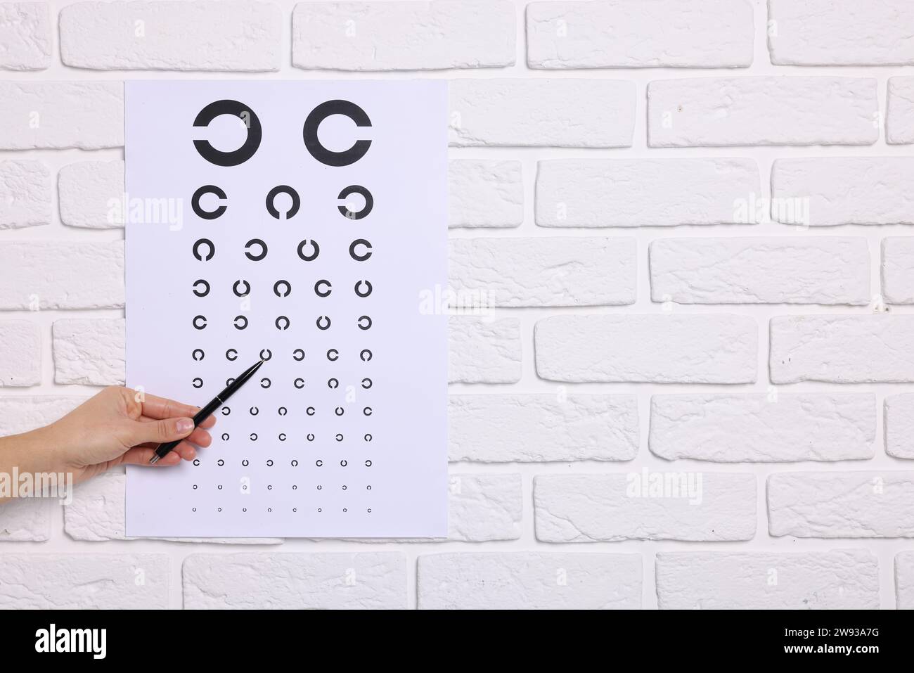 Ophthalmologist pointing at vision test chart on white brick wall ...