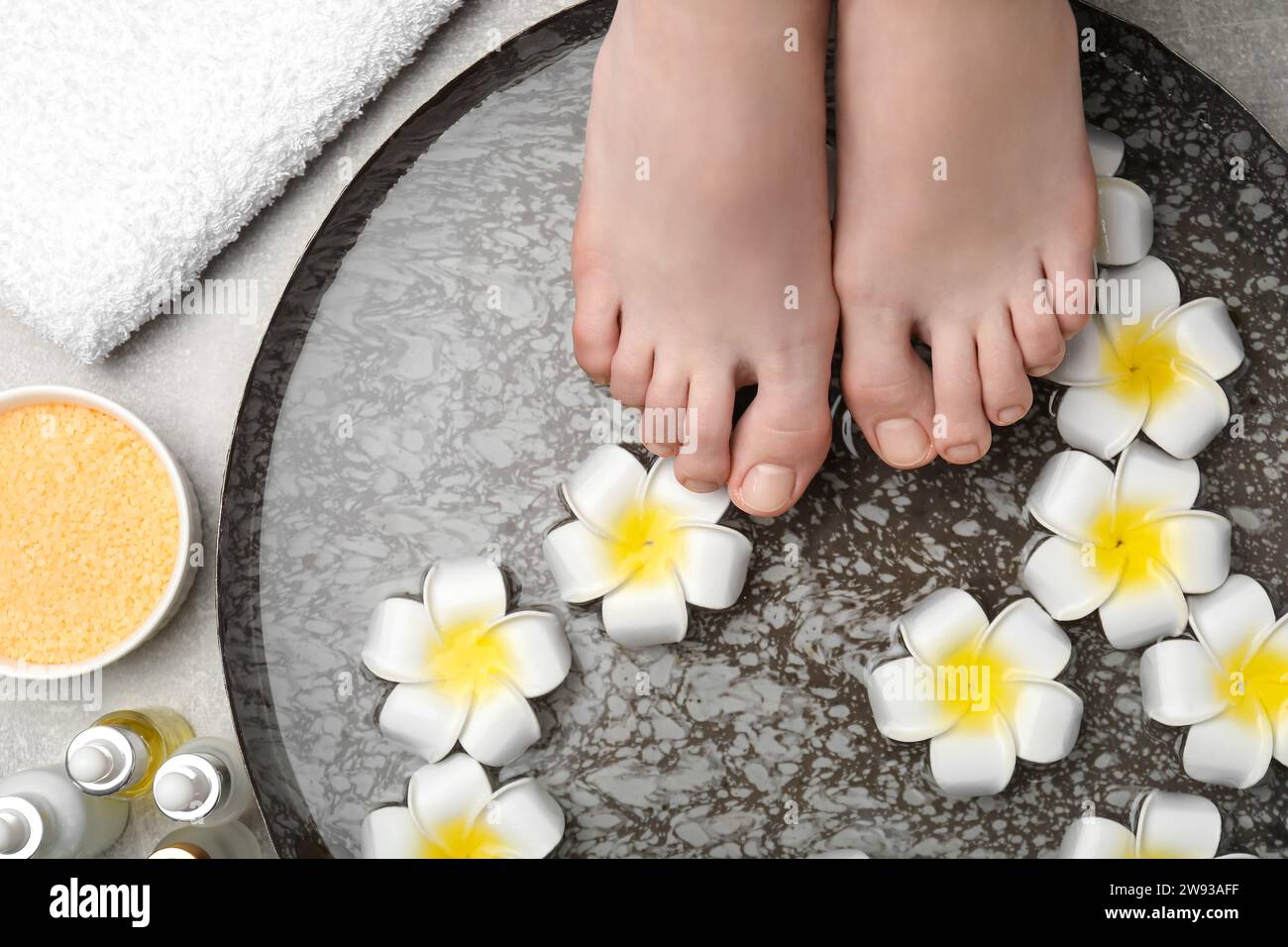 Woman Soaking Her Feet In Bowl With Water And Flowers On Light Grey